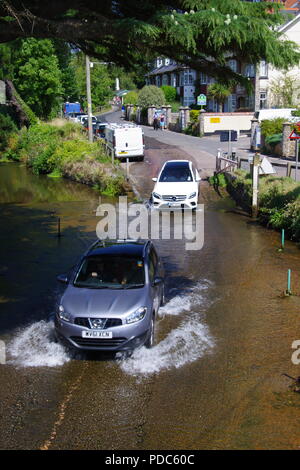 Vehicle driving through a ford across the road and splashing water ...