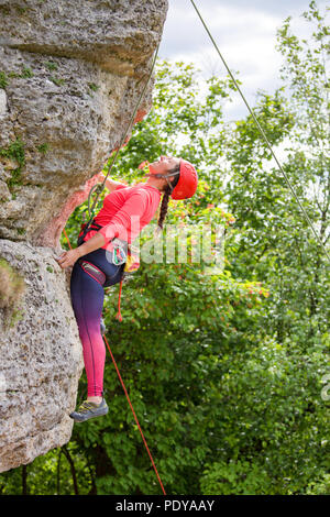 Photo of athlete girl clambering over rock against background of green ...