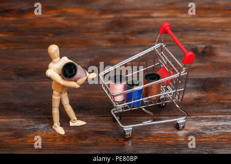 Wooden dummy puppet and mini shopping cart with thread spools. Abstract ...