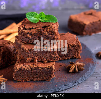 Baked pieces of chocolate brownie pie on black table, delicious dessert ...