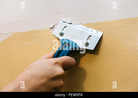 Close-up. A man with a scraper removes the old covering from the wall ...