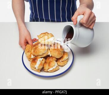 Pouring white cream sauce over pieces of fried chicken meat in pan ...