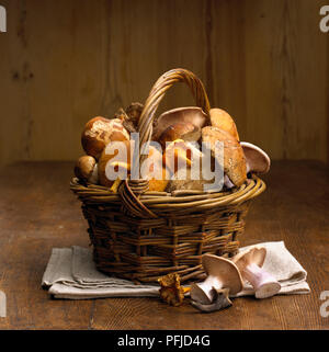 Fresh brown mushrooms in wicker basket with tomatoes and oil on wooden ...