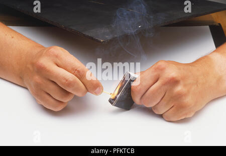 Lighting a match. Close-up of hands, matchbox and match on light-gray ...