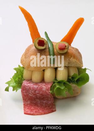 A bread roll made into a monster face with olives, cucumber and salami ...