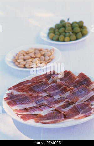 Spanish jamon serrano ham, olives and salami in a plate in a red table ...