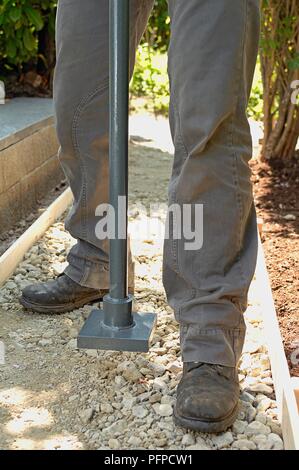 Close-up of a man tamping down sand in newly dug area for a new pond ...