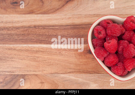 Fresh raspberries in heart shaped bowl with rose and green leaves on ...