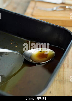 Tilting roasting tin and skimming fat off top of the juices, using a ...