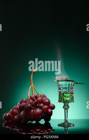 crystal glass of absinthe with branch of grapes and burning sugar on ...