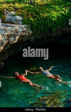 Two young women floating on their backs in a bright blue swimming pool ...