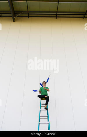 Acrobat wearing sunglasses, sitting on ladder, juggling Stock Photo - Alamy