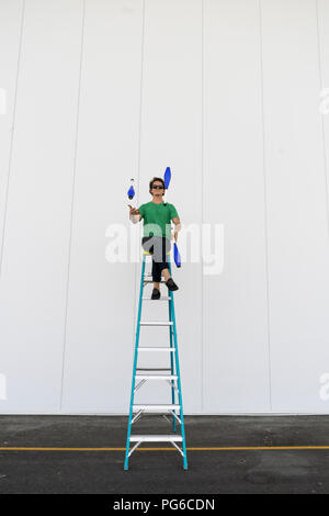 Acrobat wearing sunglasses, sitting on ladder, juggling Stock Photo - Alamy