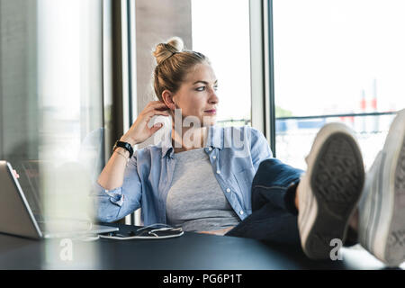 Young businesswoman sitting with feet on desk talking on cell phone ...