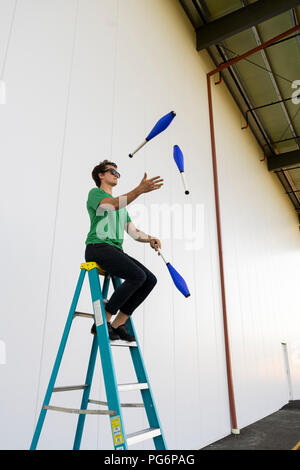 Acrobat wearing sunglasses, sitting on ladder, juggling Stock Photo - Alamy