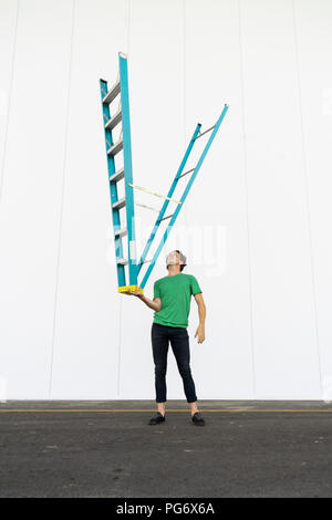 Acrobat balancing ladder upside down in his hand Stock Photo - Alamy