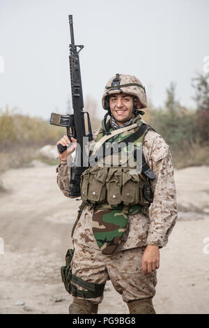 Smiling armed soldier posing with assault rifle, looking camera indoors ...