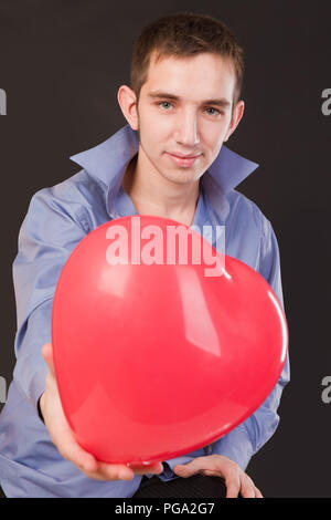 Young guy holding a red heart-shaped balloon Stock Photo - Alamy