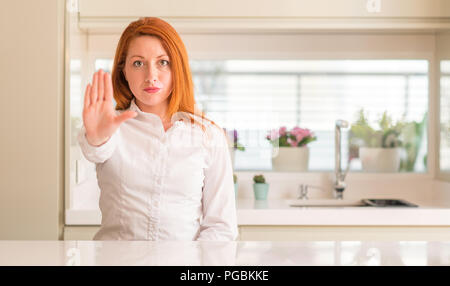 Redhead woman at kitchen with serious expression on face. Simple and ...