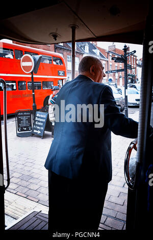 Old Fashioned type of Bus Conductor holding on to the rail of the rear ...
