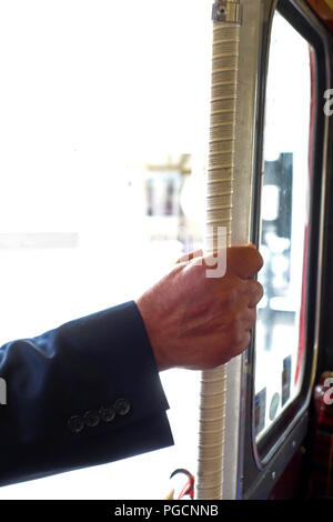 Old Fashioned type of Bus Conductor holding on to the rail of the rear ...