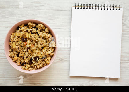Pink bowl of fruit granola and blank notebook on white wooden table ...