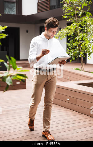 Walking, holding notepad. Handsome young man is on agricultural field ...