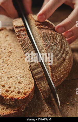 Female baker cutting rye bread at table in kitchen Stock Photo - Alamy