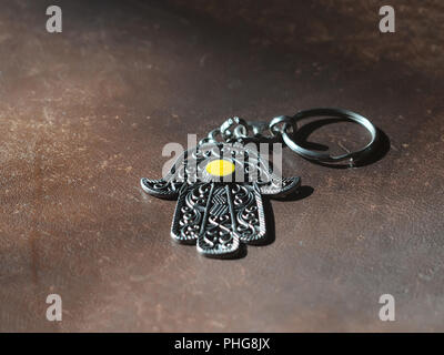 A key ring in the form of Fatima Hand on a brown leather background ...