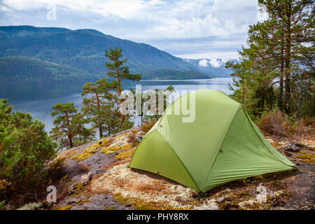 Tent camping on a Norwegian fjord with dark clouds and snow-covered ...