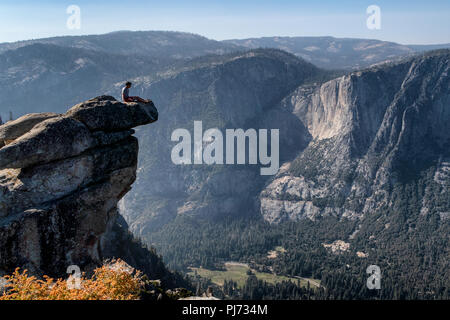 A sits on an overhanging rock at Glacier Point enjoying the ...