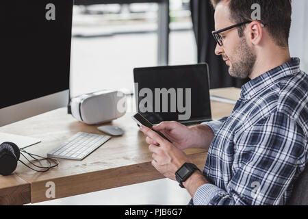 handsome young programmer in eyeglasses smiling at camera while sitting with hands behind head ...