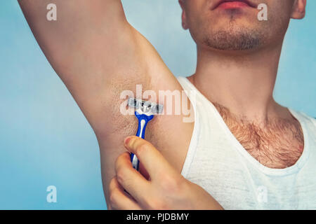 Male depilation. Young attractive man using razor to remove hair from ...