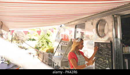 Female waitress writing menu on menu board while using digital tablet ...
