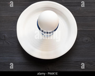 above view of white egg in cup on plate on dark wooden table with blank ...