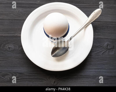 above view of white egg in cup on white plate on dark wooden table ...