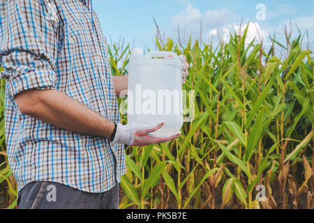 Farmer holding pesticide chemical jug in cornfield. Blank unlabeled ...