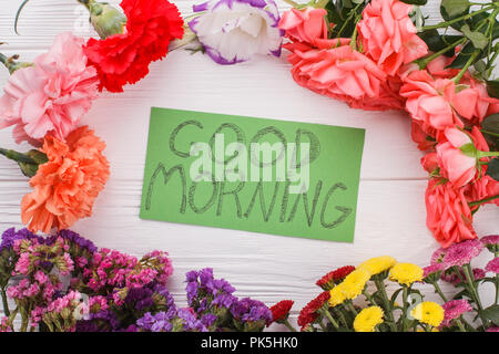 Rose flowers and good morning wish in notepad. Close up. White wooden ...