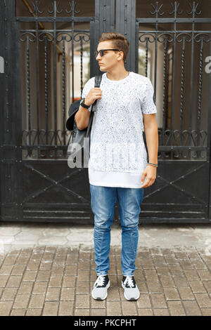 young man with cap and blue shirt is standing in front of mountain lake ...