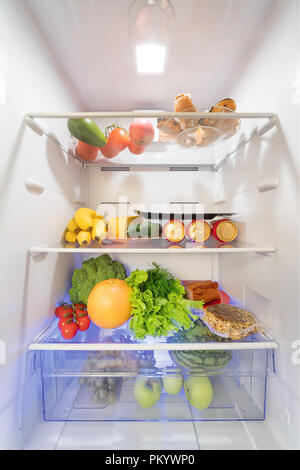 A fridge full of beer and vegetables, the refrigerator door open ...
