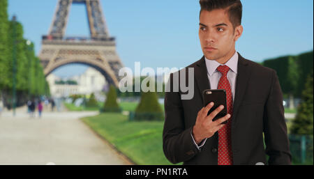 Portrait of cute Hispanic businessman texting on cellphone near Eiffel ...