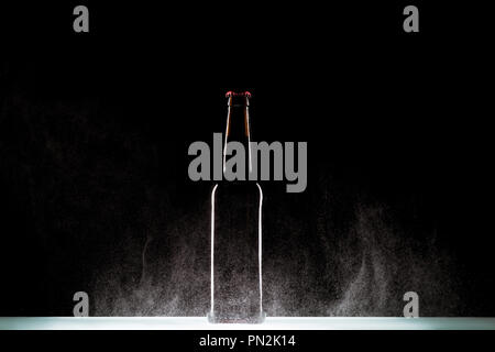 beer bottle with spraying water around at surface on black background ...