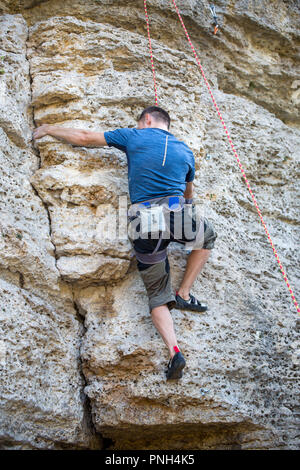 Young man climbs up an outdoors rock wall Stock Photo - Alamy
