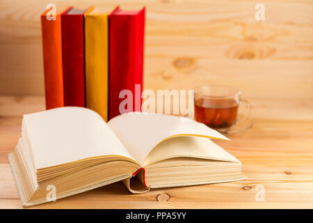 Open book and glass cup of tea and a stack of books with colorful ...