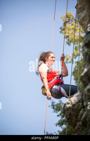 Photo of athlete girl clambering over rock against background of green ...