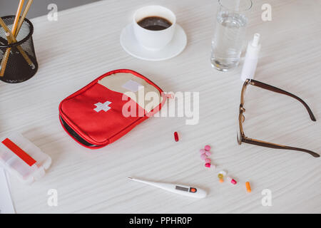 first aid kit, pills, glasses and glass of water on table in office ...