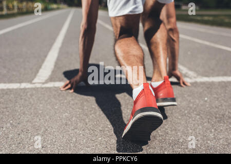 partial view of male sprinter in starting position on running track ...