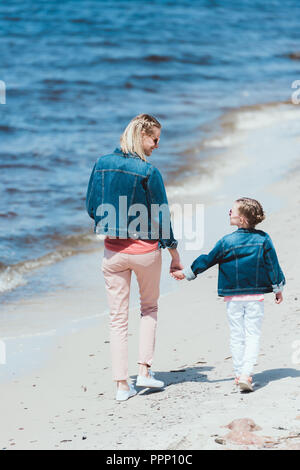 back view of stylish mother and daughter standing at paddock with horse ...