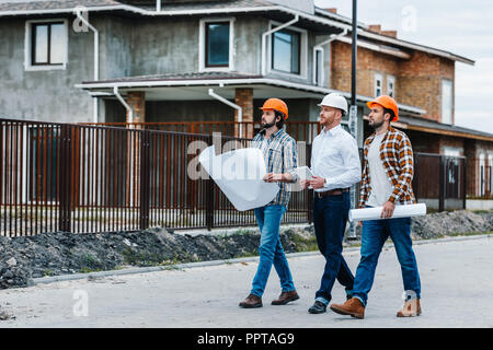 group of architects walking by constructing street with blueprints ...