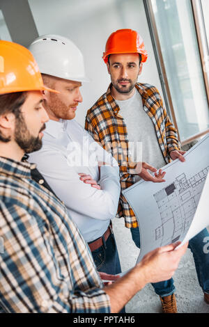 group of architects with blueprint having conversation inside of ...